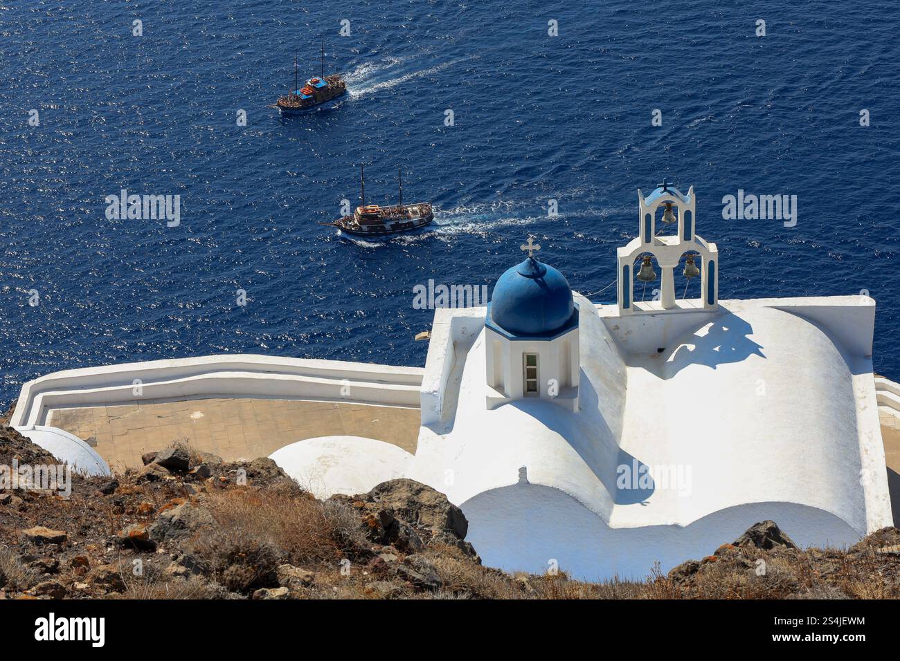 A whitewashed church with a blue dome and three traditional bells, two ...