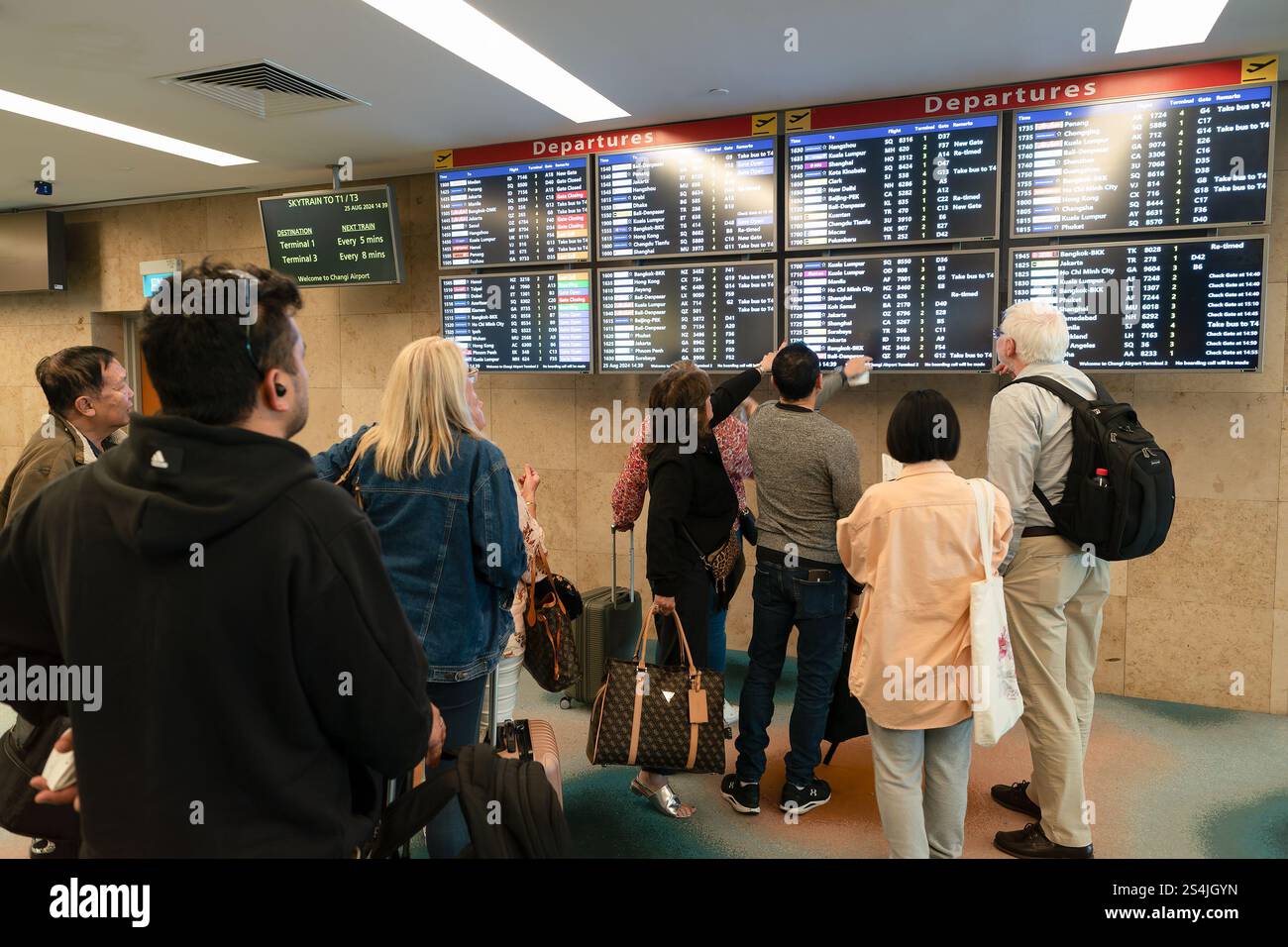 SINGAPORE - AUGUST 25, 2024: passengers stand in front of the FIDS ...