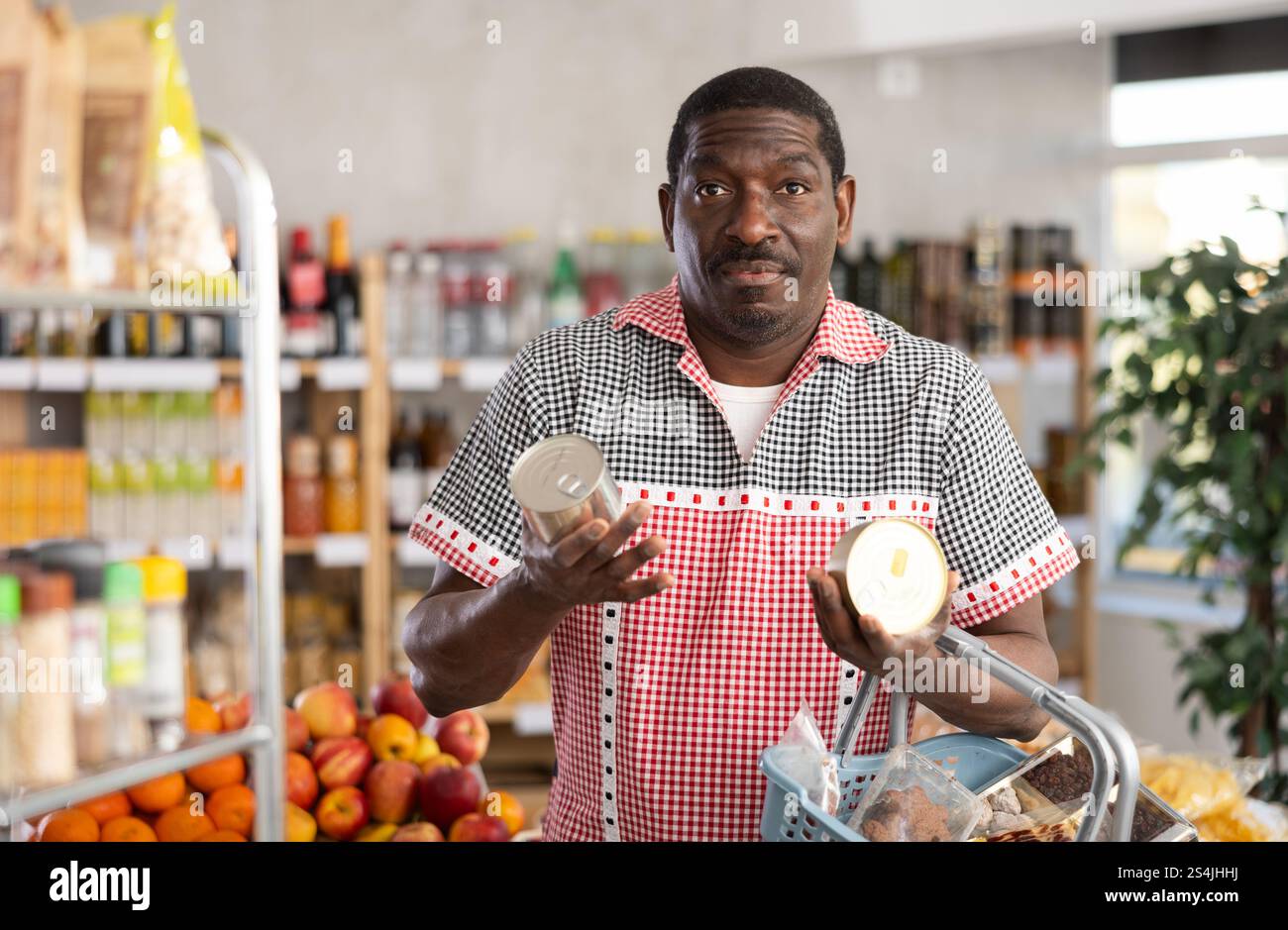 African man is holding two tin cans of preserves in hands, choosing ...