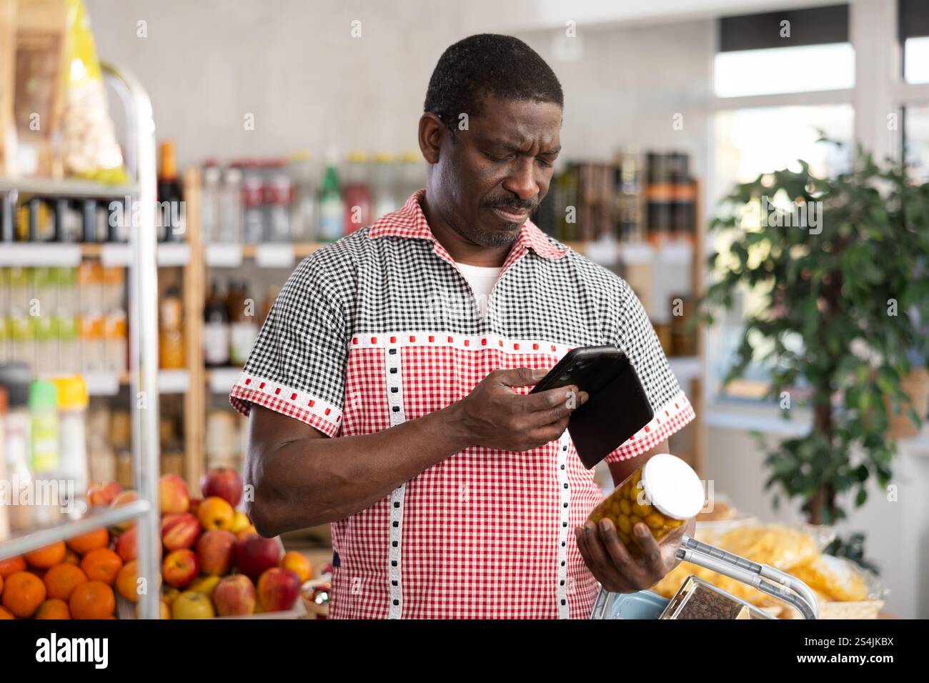 African man customer holds jar of canned olives in hand, scans QR code ...