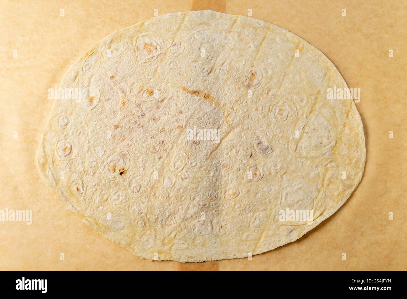 A large, round tortilla rests on a sheet of parchment paper. Its ...