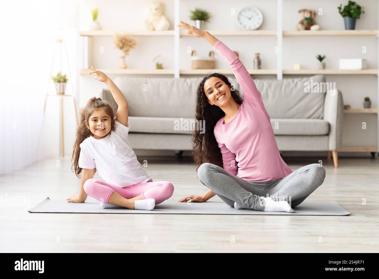 Sporty mother and daughter sitting on fitness mat, stretching Stock ...
