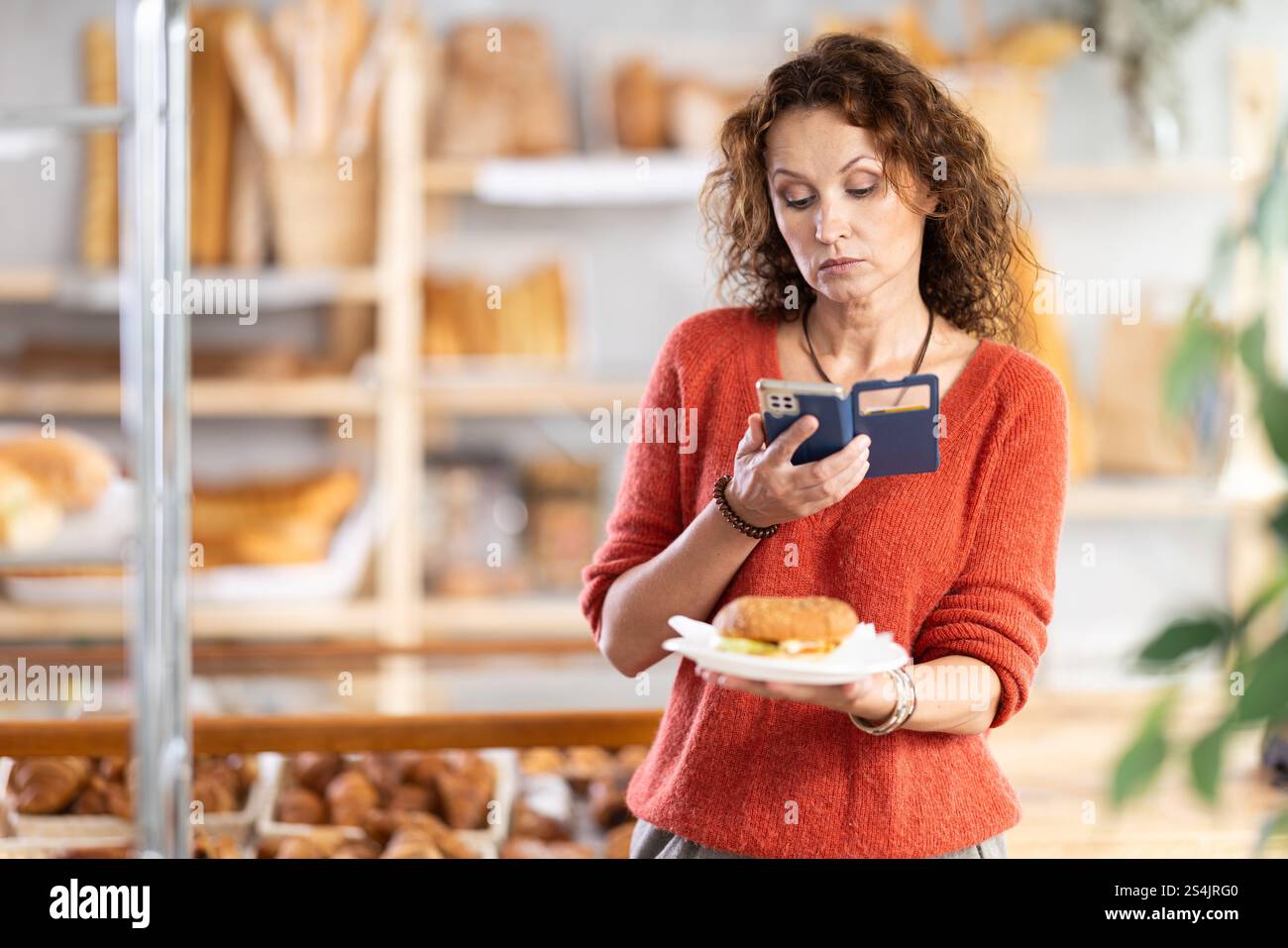 European female customer with phone takes pictures of burger croissant ...