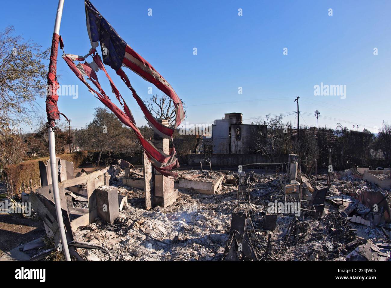 An American flag is seen tattered as it flies above a burned down home ...
