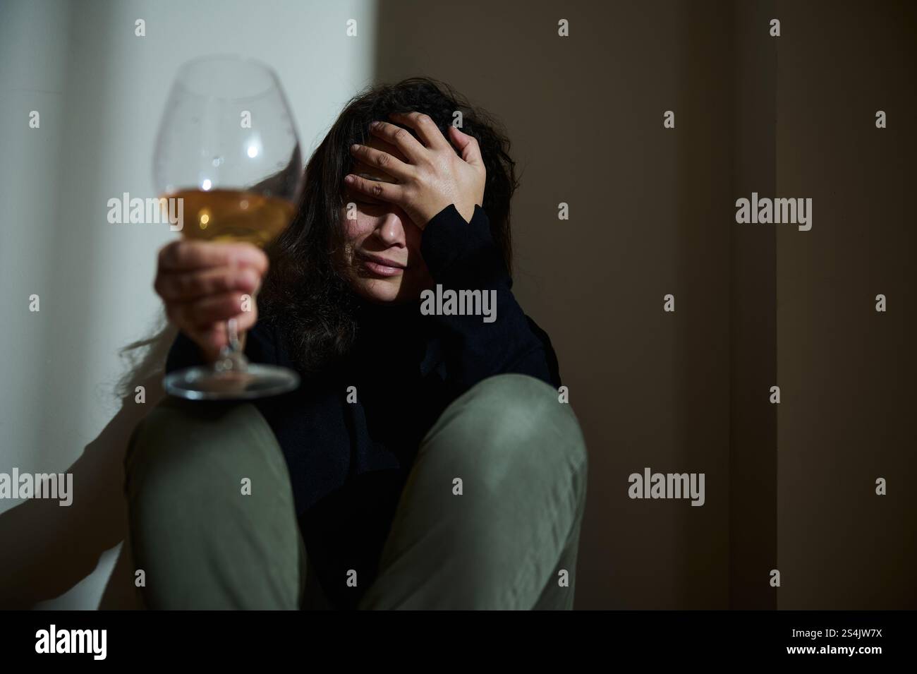 A seated individual holds a glass of wine with a somber and reflective ...