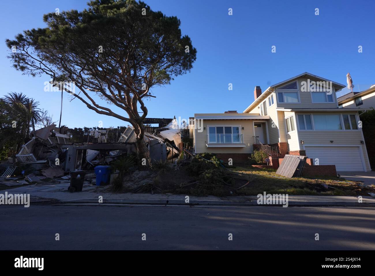 An intact house stands next to a home destroyed by the Palisades Fire ...
