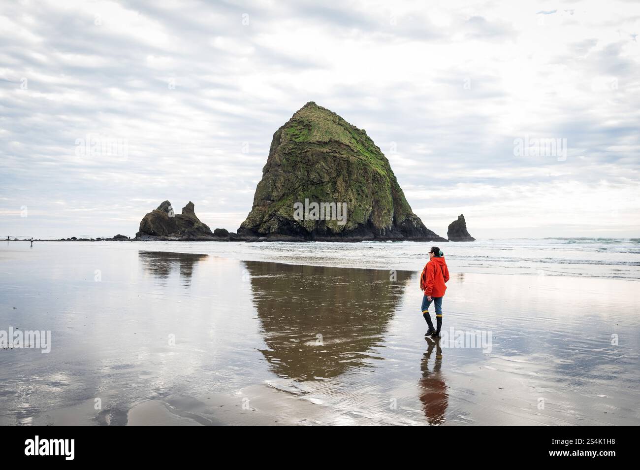 A woman walks on Cannon Beach in front of Haystack Rock, Oregon. Along ...