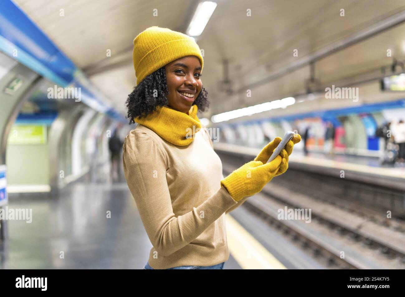 Young black woman wearing yellow winter clothes and gloves using her ...