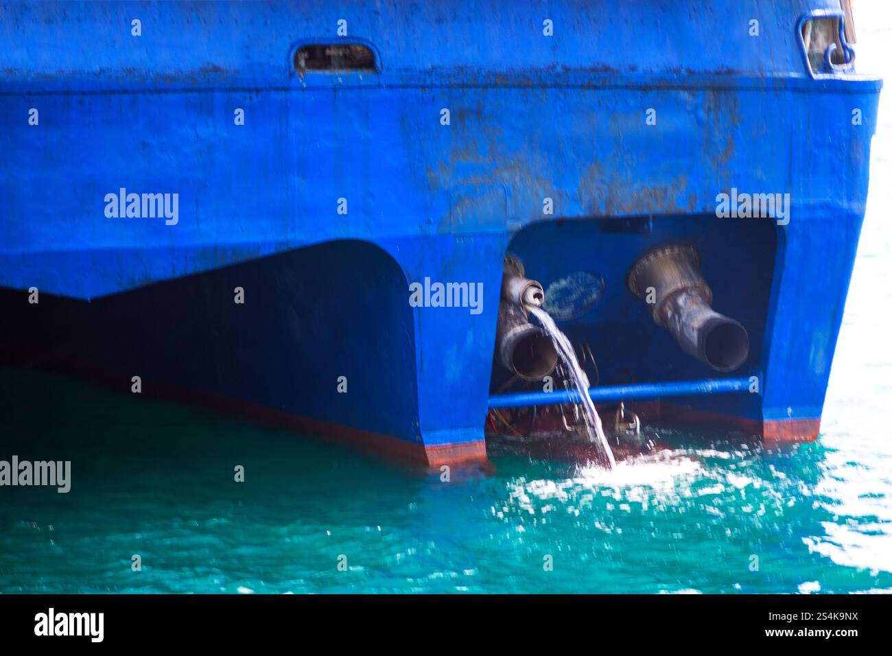Stern of blue ship with water being discharged from two large pipes ...