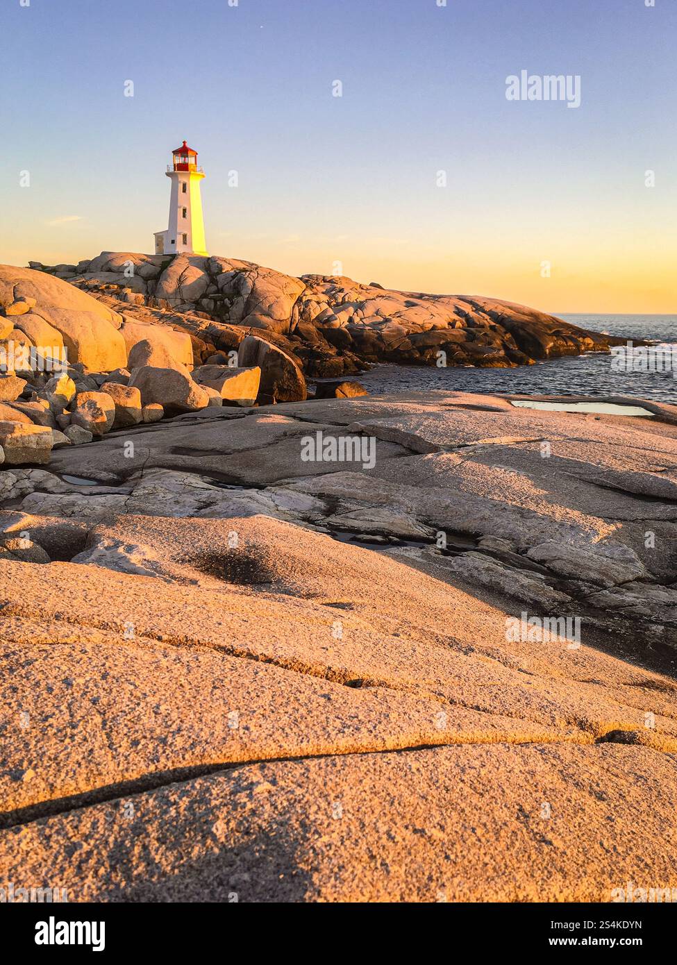 Sunset by the coast at Peggy's Cove lighthouse in Nova Scotia. This ...