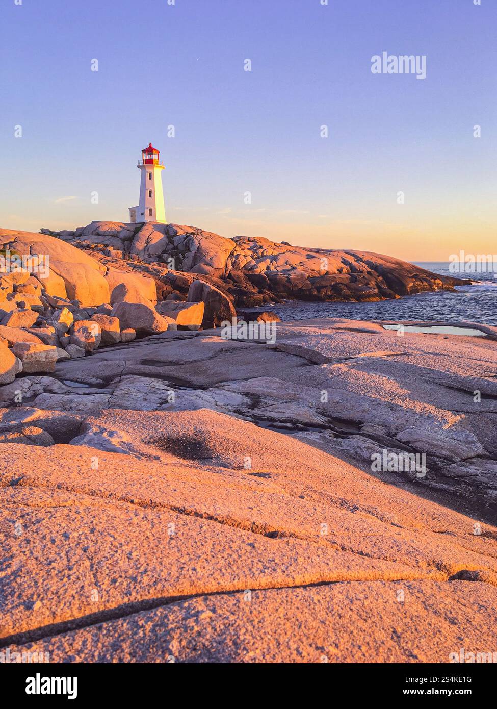 Sunset by the coast at Peggy's Cove lighthouse in Nova Scotia. This ...