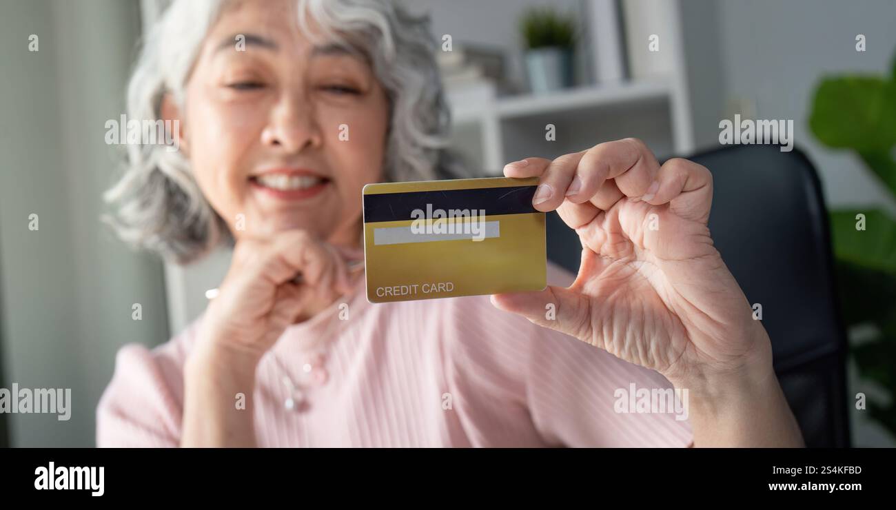 Elderly woman proudly displaying her credit card after successful online shopping at home Stock ...
