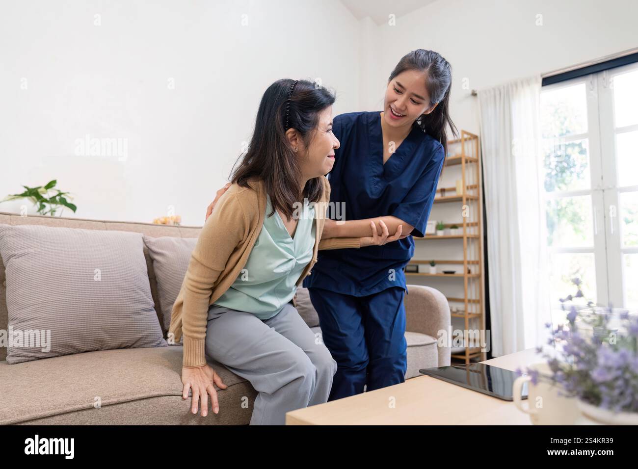 Dedicated caregiver assisting elderly client as she stands up from the ...