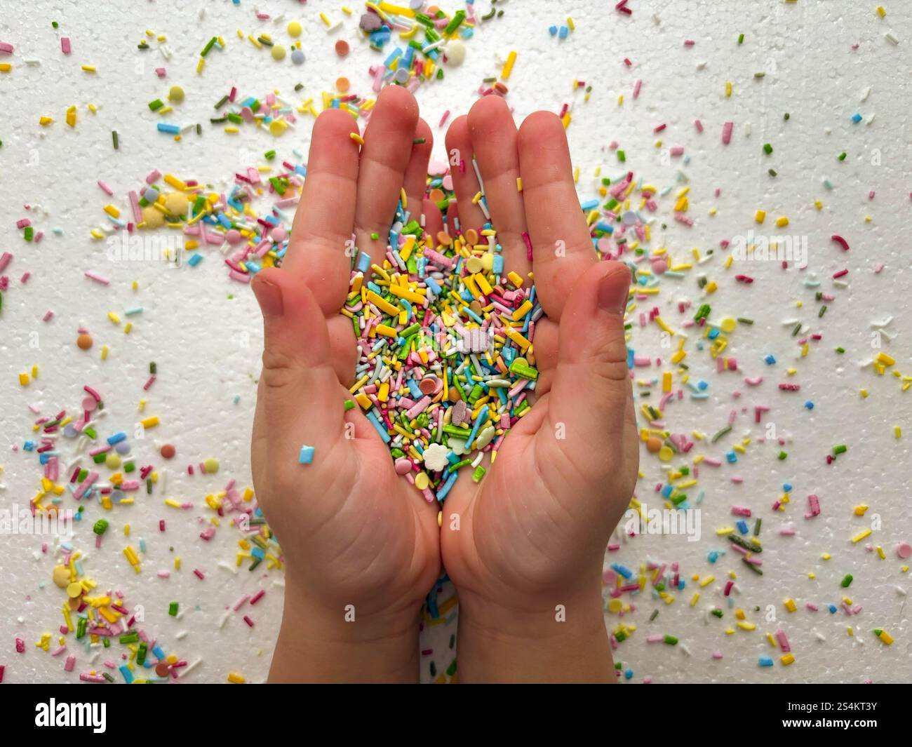 Child playing with colored sugar candies on white background ...