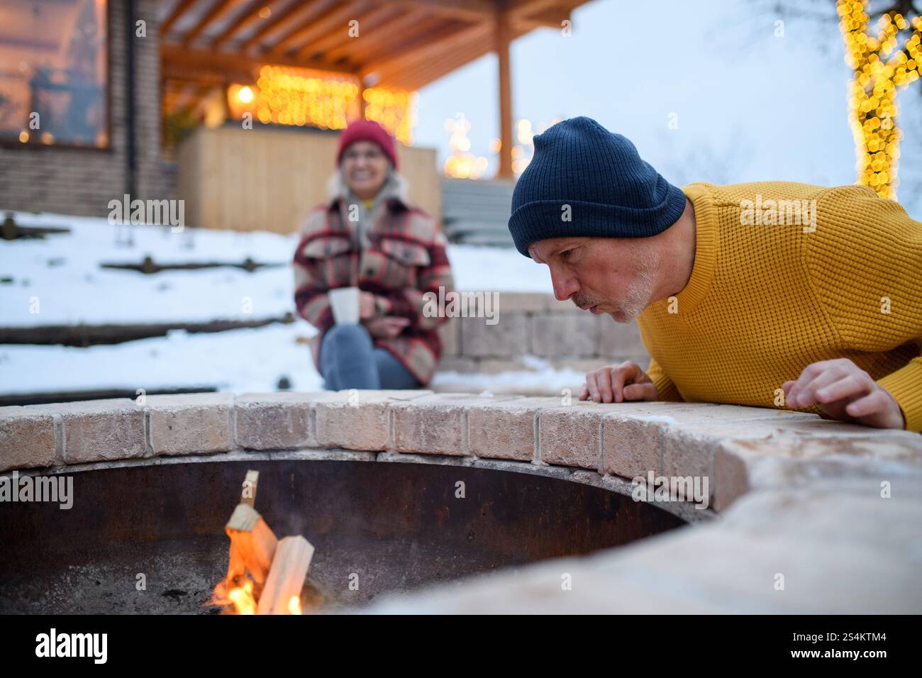 Older man starting fire in garden fire pit. Seniors watching flames ...