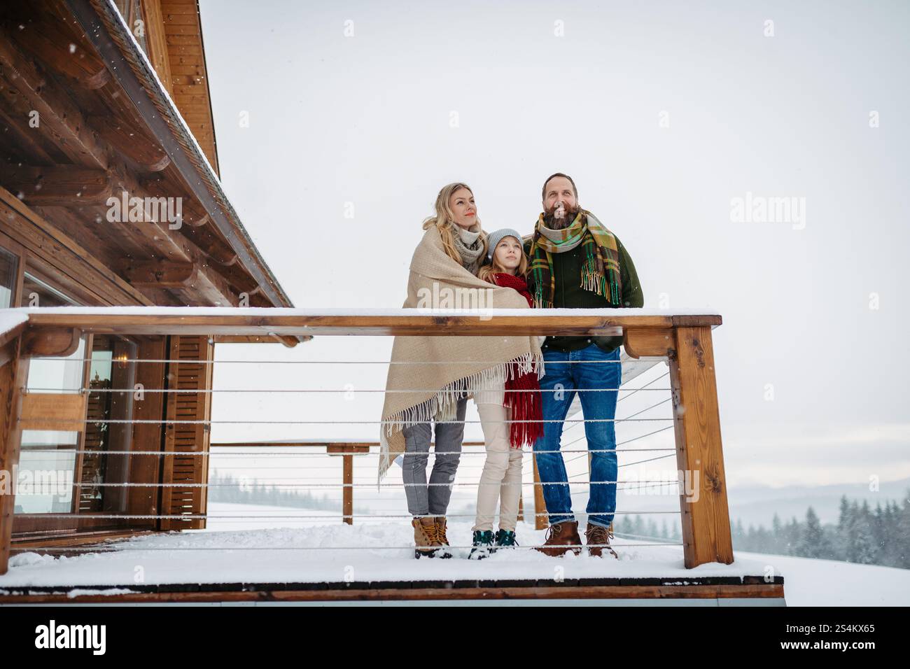 Family standing on the snowy cabin balcony, looking at beautiful winter ...