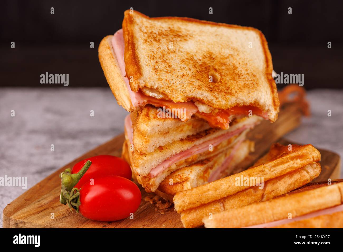 A charming half-eaten egg, ham, and cheese sandwich sits atop a ...