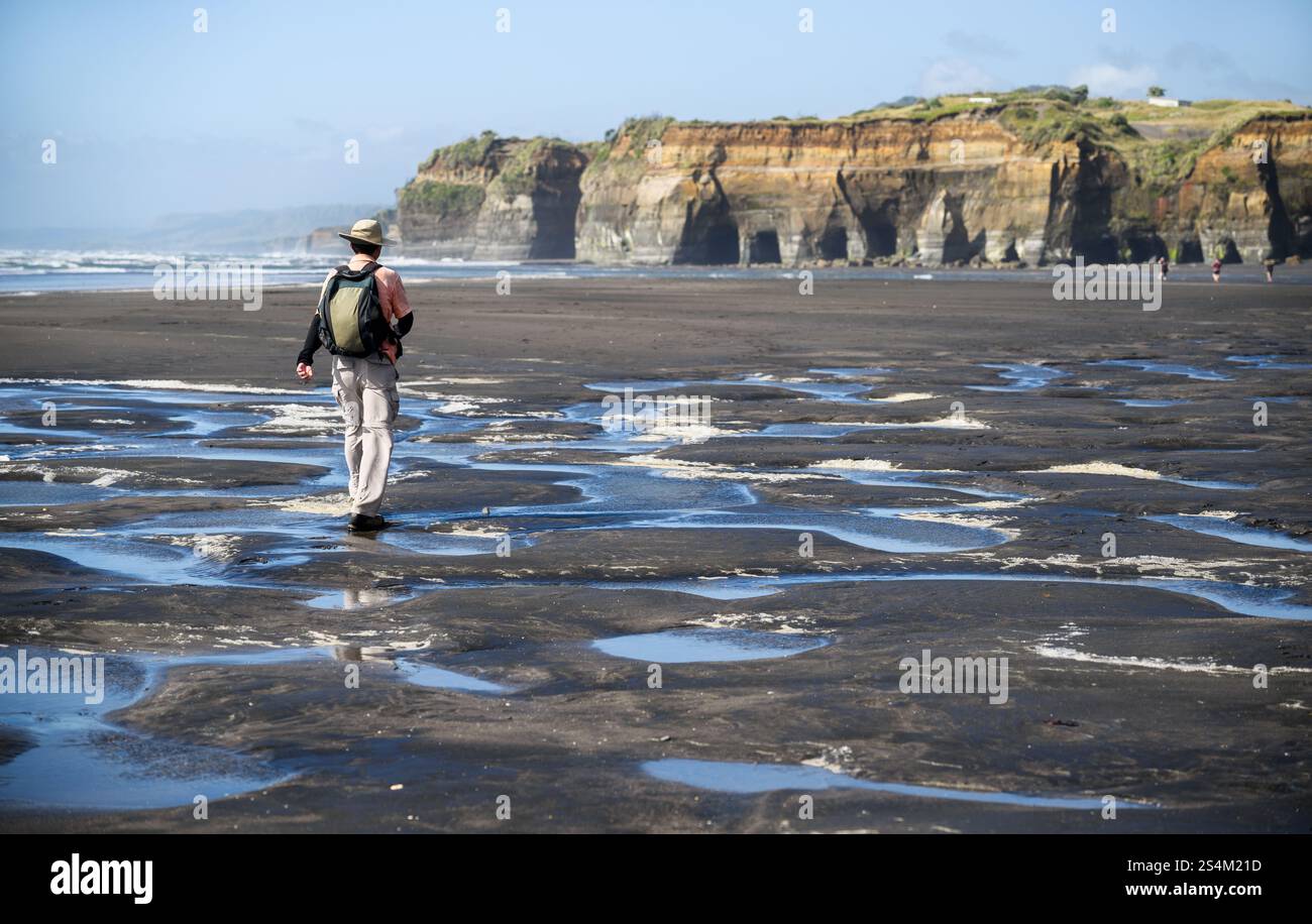 Man walking on Tongaporutu beach. Puddles of water scattered on the ...