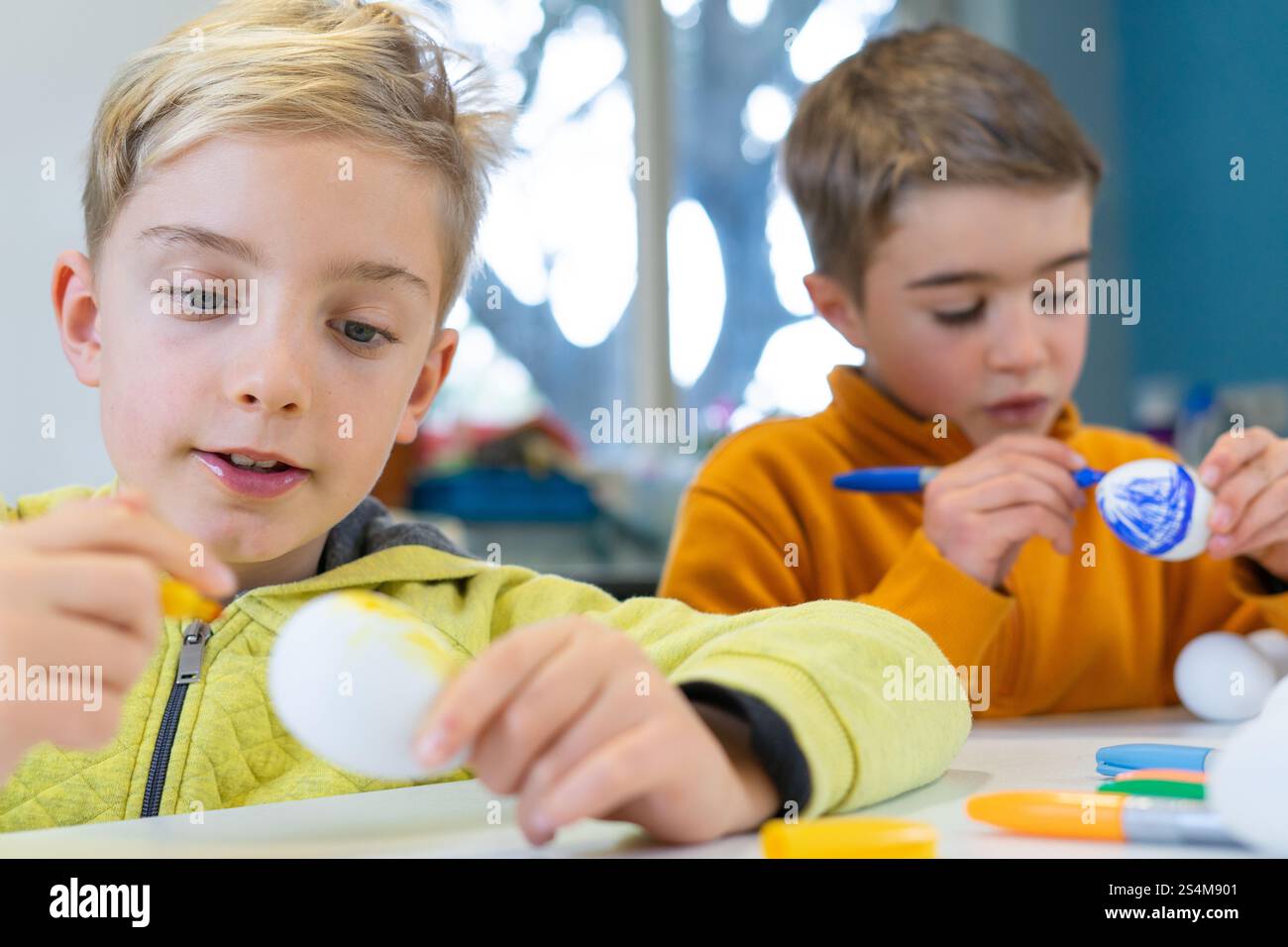 Two students are painting easter eggs at school using colored markers ...
