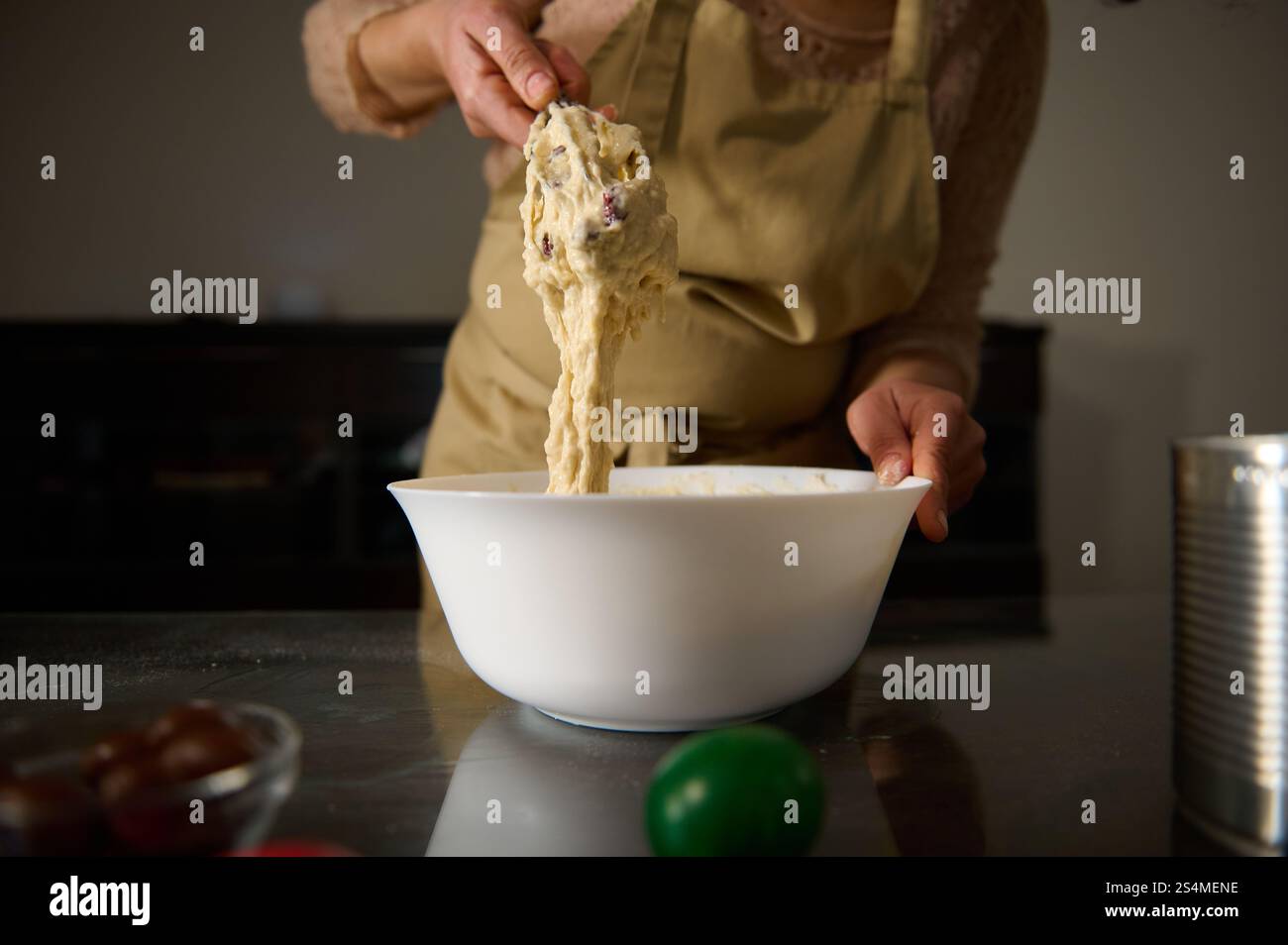 A person dressed in an apron kneads dough in a white bowl, evoking ...