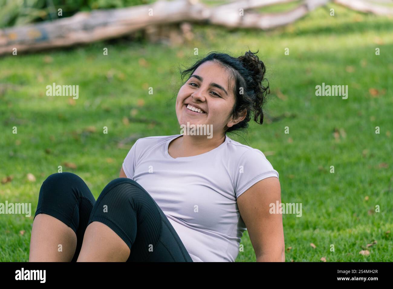 A cheerful Latina woman rests on the grass in a Bogota park, enjoying a ...