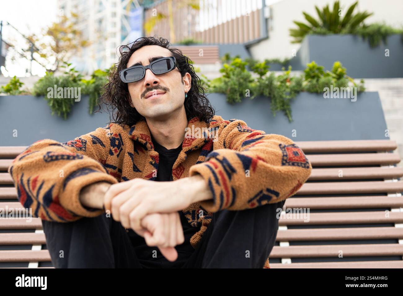 Stylish man with sunglasses and patterned jacket sits relaxed on a ...