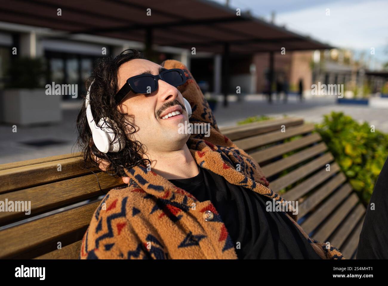 A man with a mustache lounges on a park bench, enjoying the sun He ...