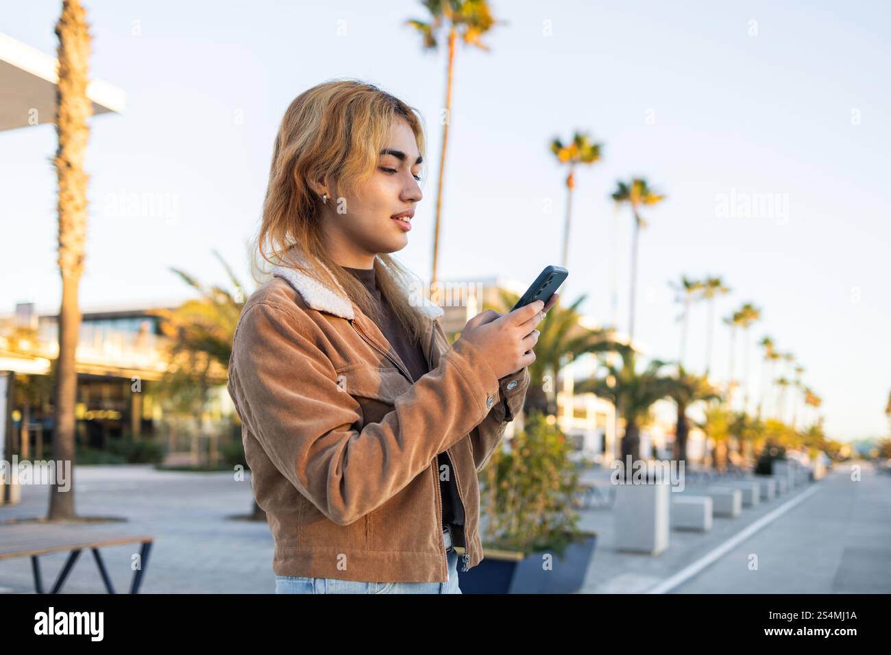 Mixed race woman in casual jacket using a smartphone outdoors She ...