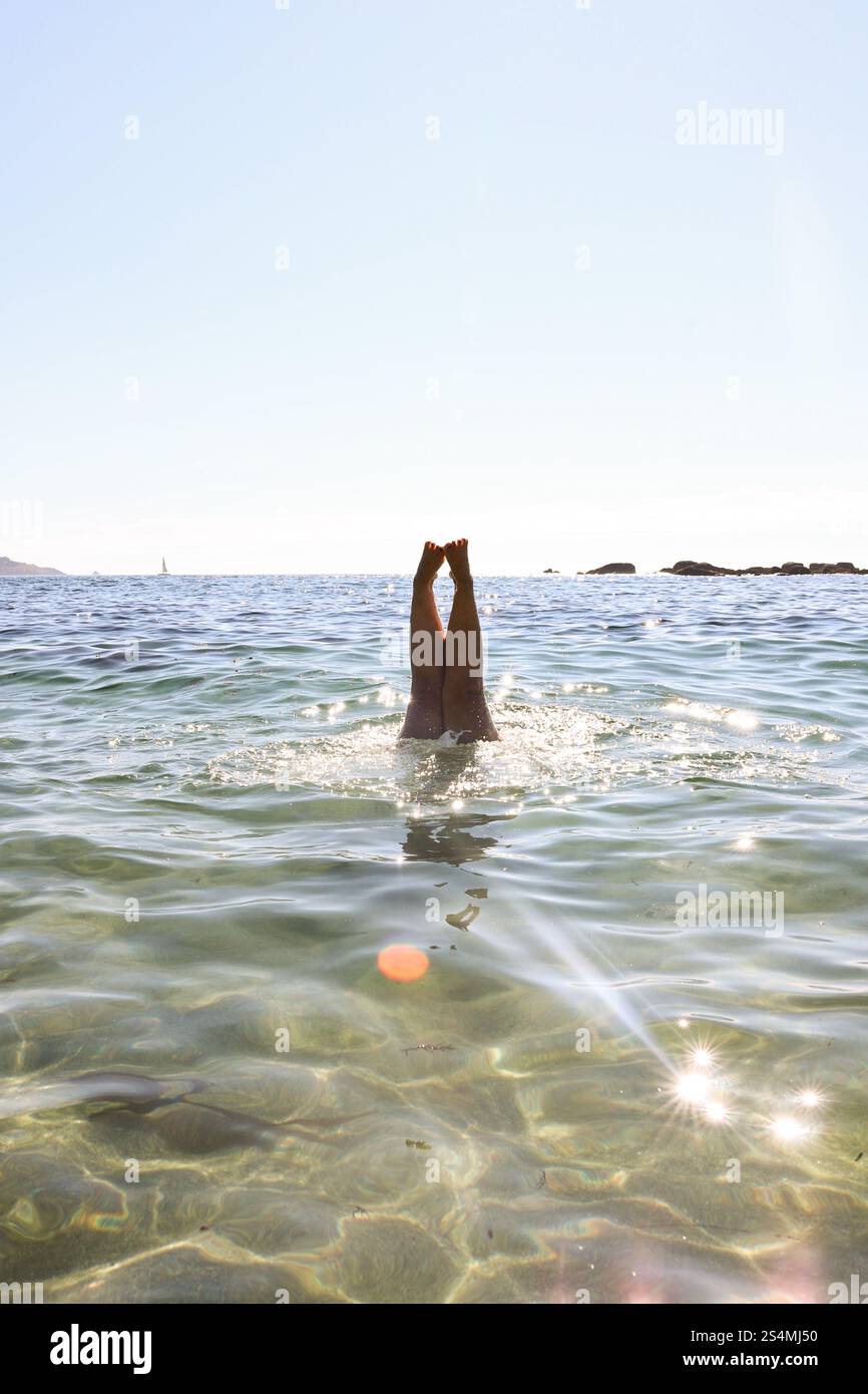 A person performs a handstand in crystal-clear ocean waters under the ...