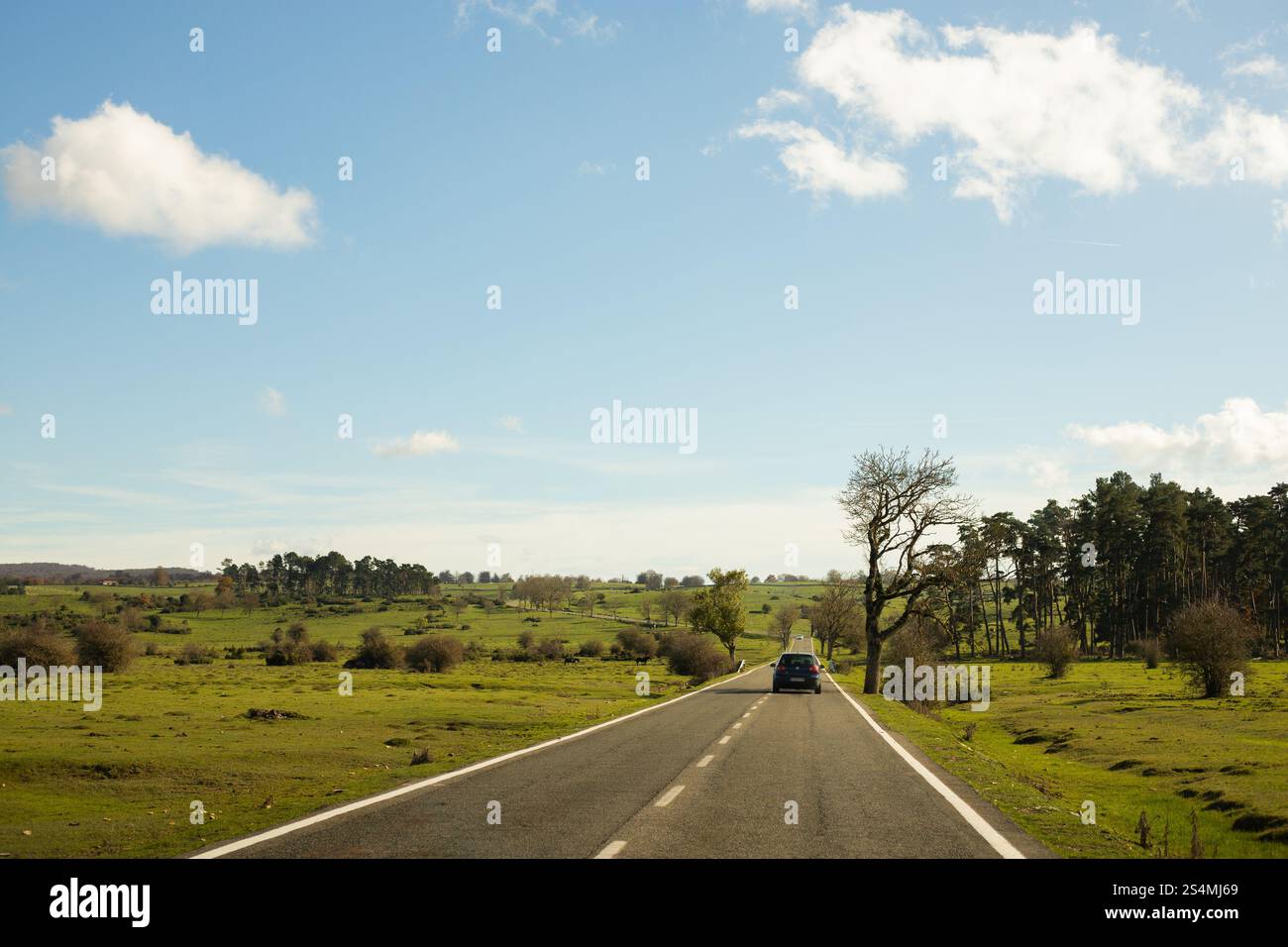 A car travels along a quiet country road under a clear blue sky on a ...