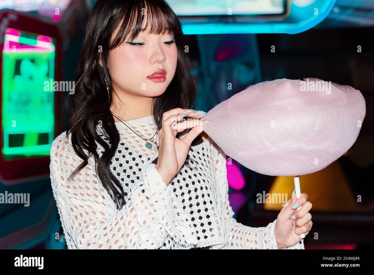 Asian Gen Z girl enjoys cotton candy in a vibrant arcade setting The ...
