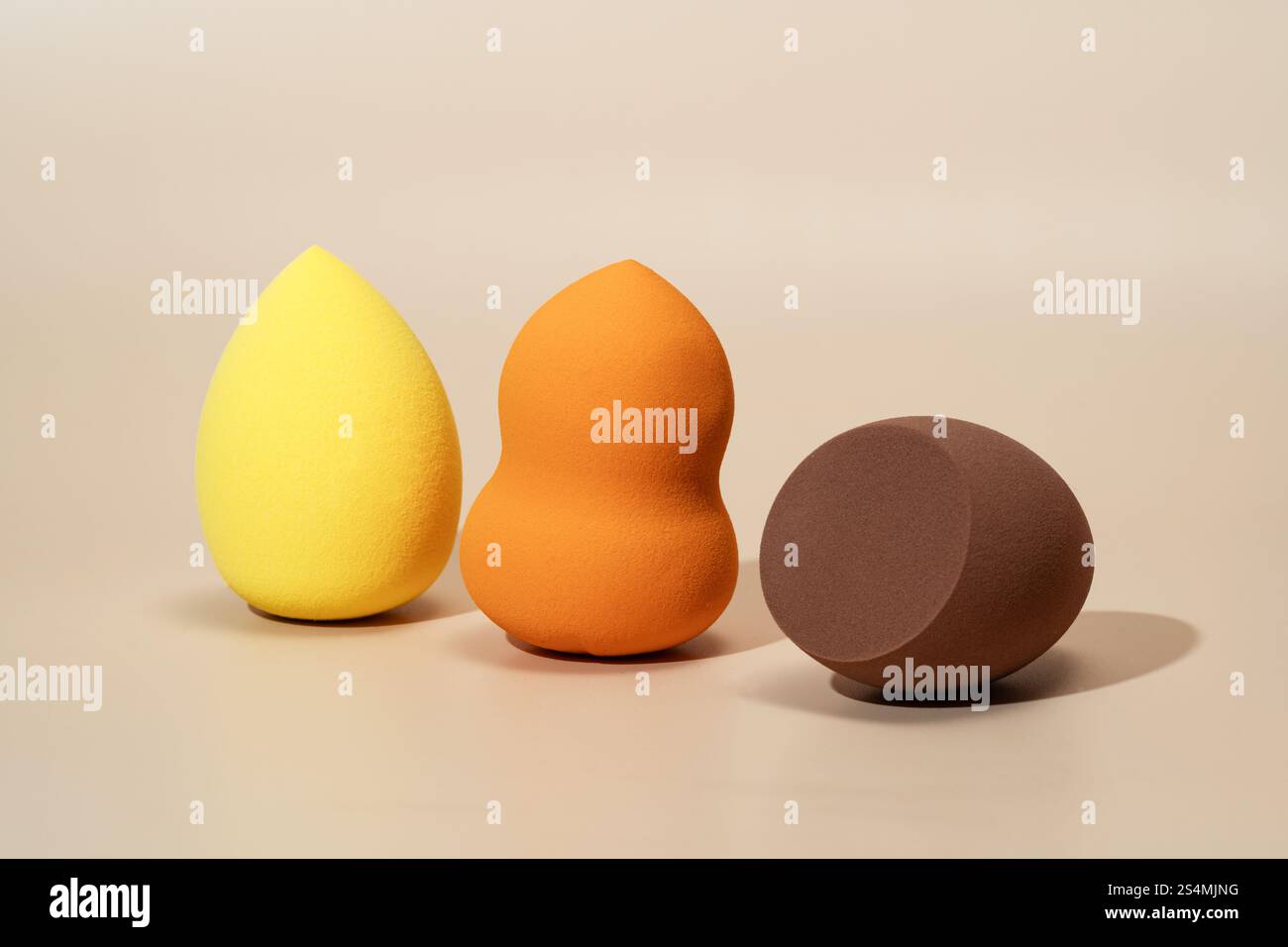 Three colorful cosmetic sponges in yellow, orange, and brown are ...