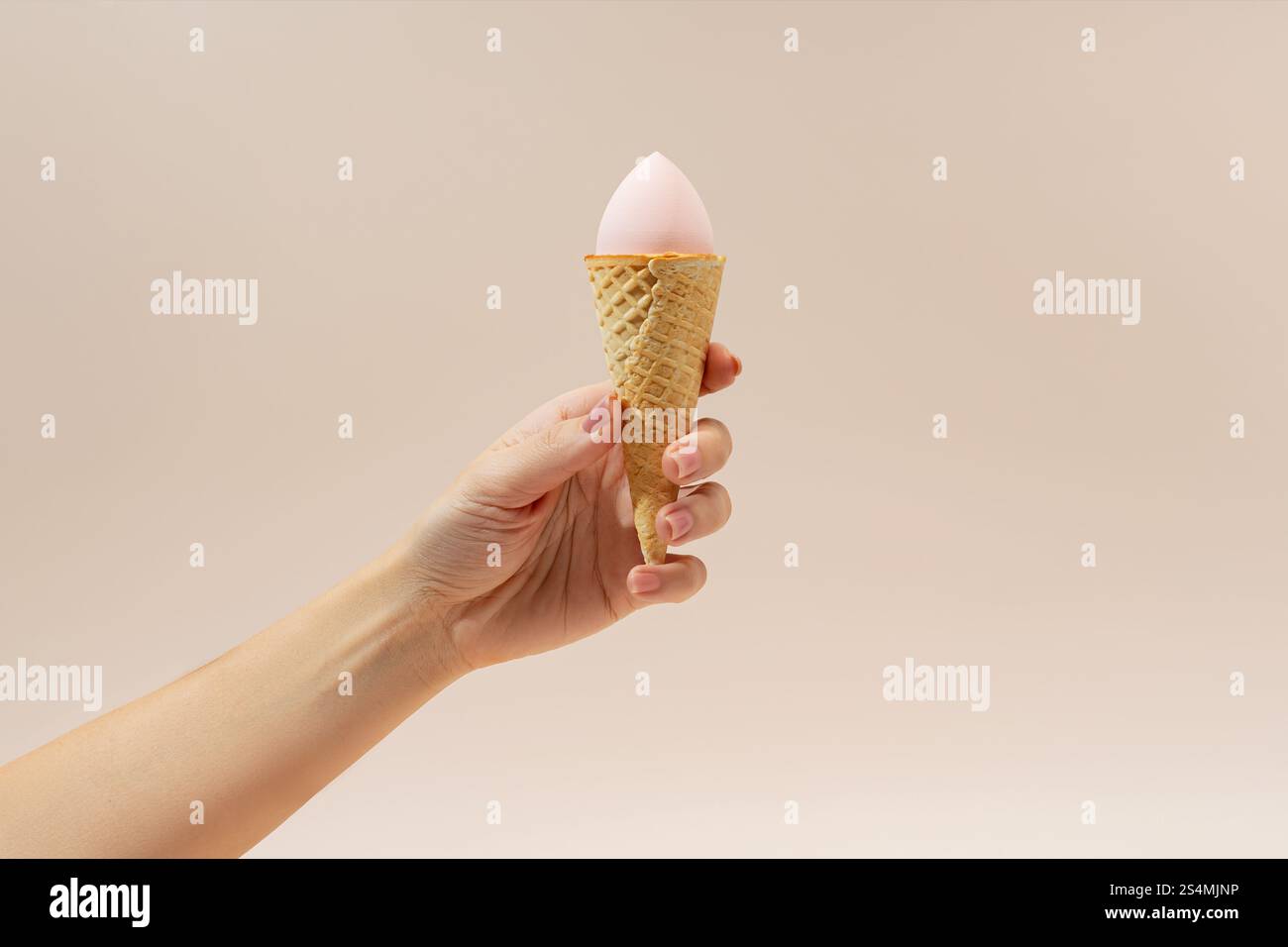 A hand holds a waffle cone with a pink cosmetic sponge inside ...