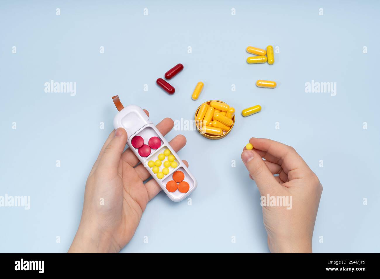 From above cropped unrecognizable hands hold a pill box and select different colored capsules ...