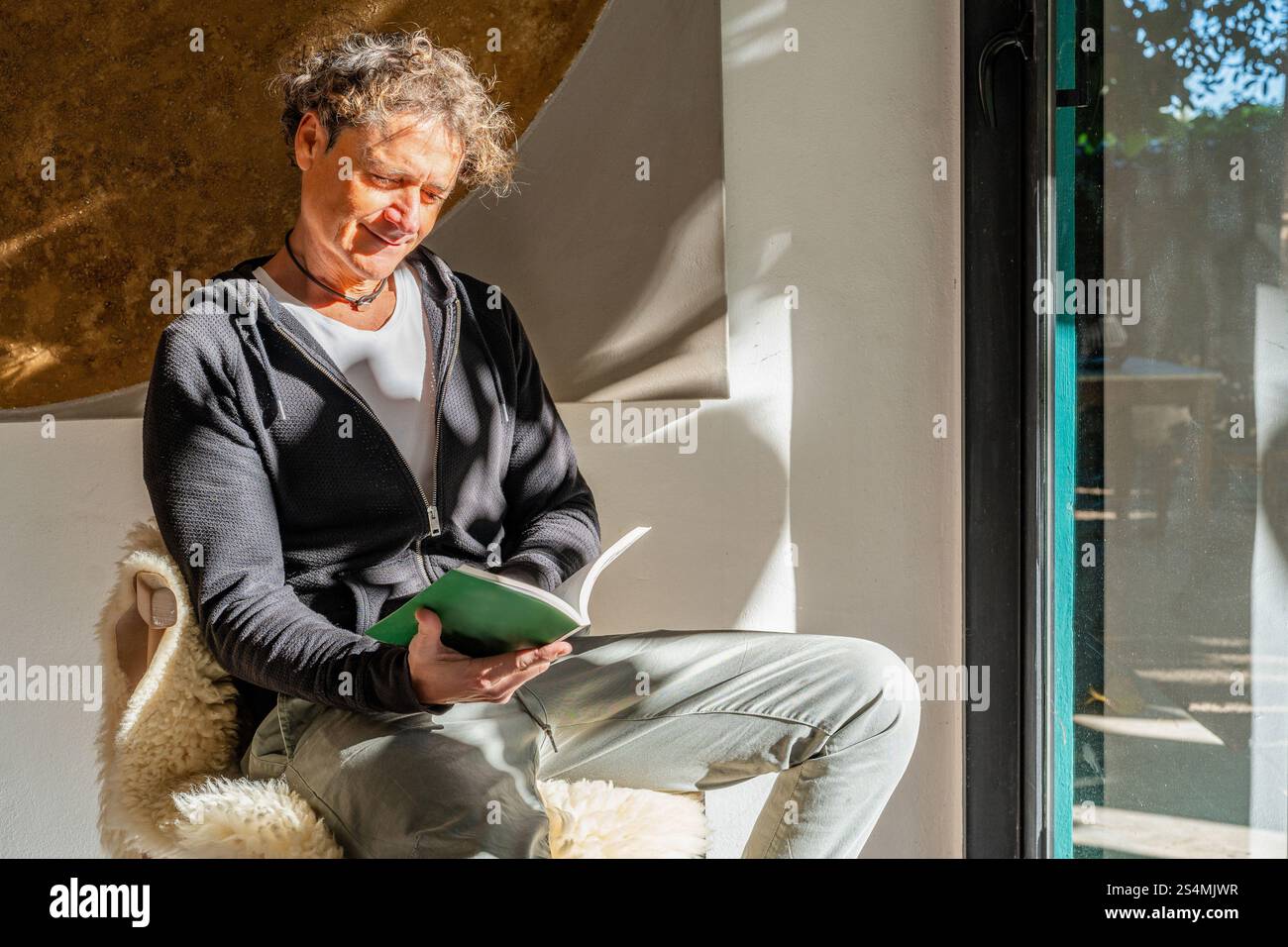 A man enjoys a quiet moment reading a book at home, sitting comfortably ...