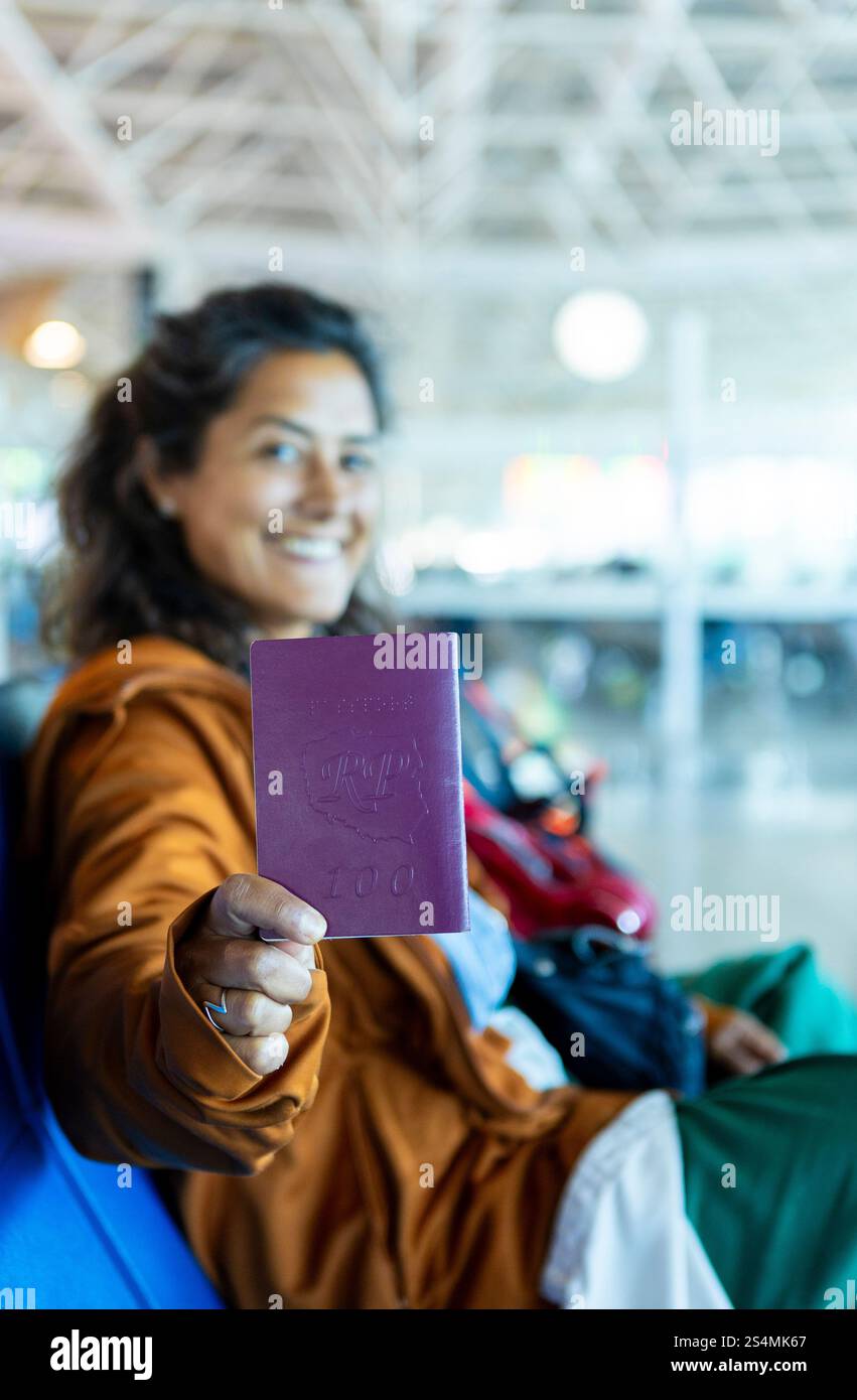 A smiling traveler at an airport terminal proudly shows their passport ...