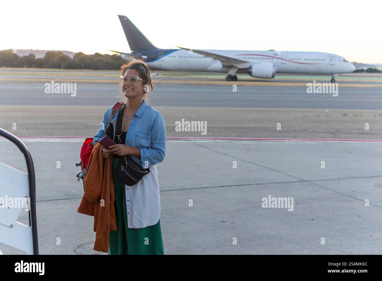A smiling traveler ready to board a flight, carrying a red backpack and ...