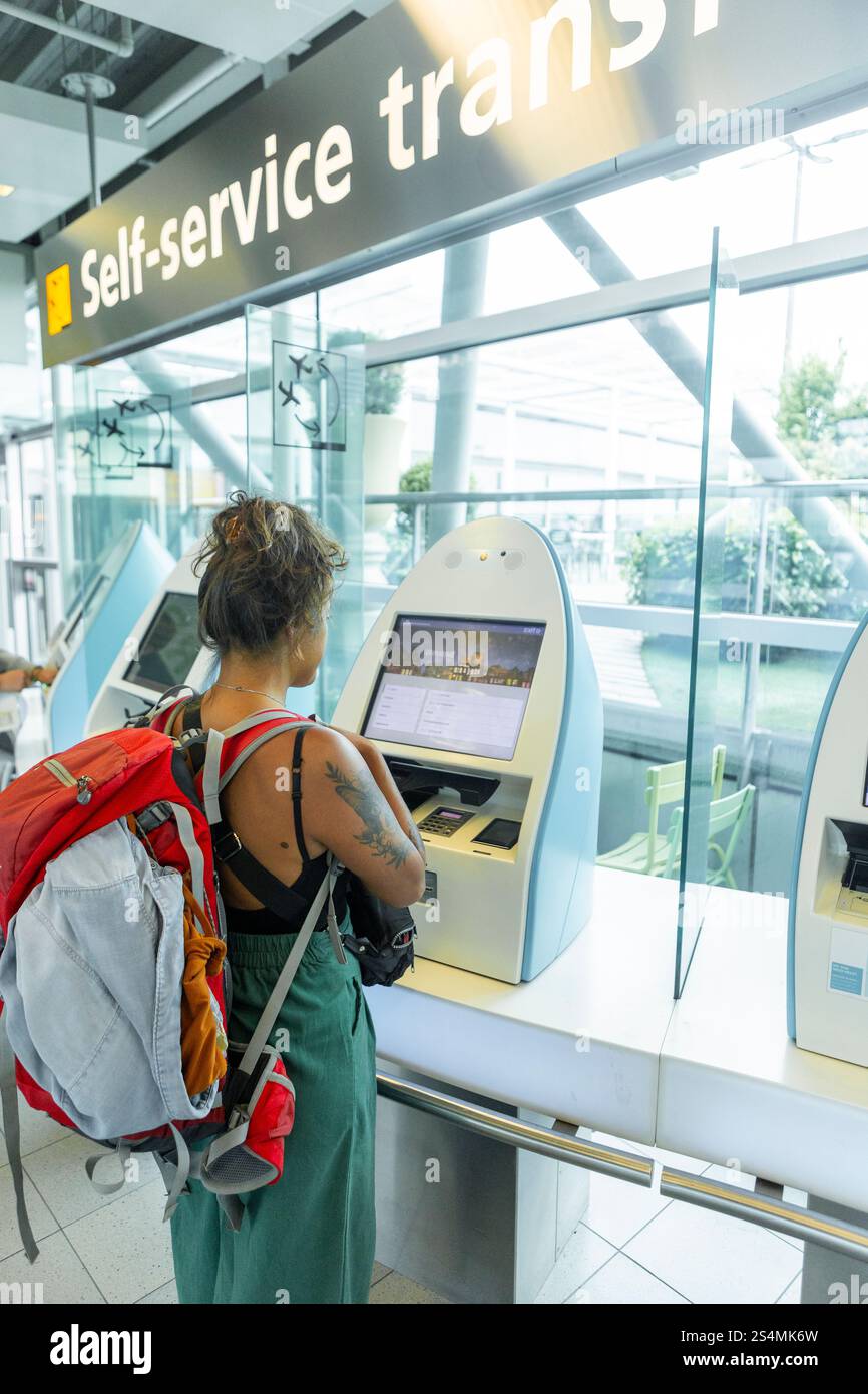A traveler with a backpack uses a self-service kiosk in an airport ...
