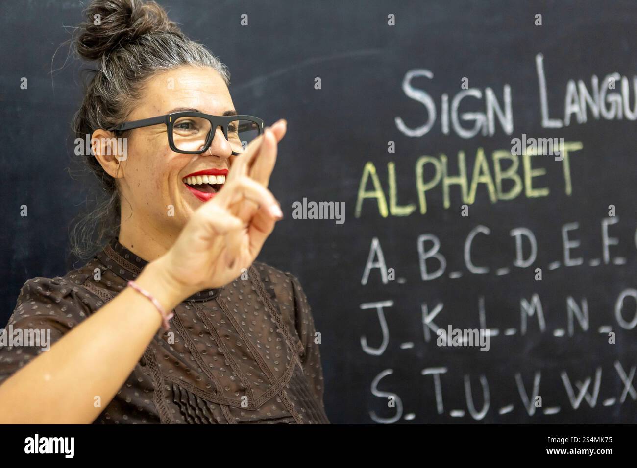A woman teaches sign language alphabet in a classroom, gesturing with a ...