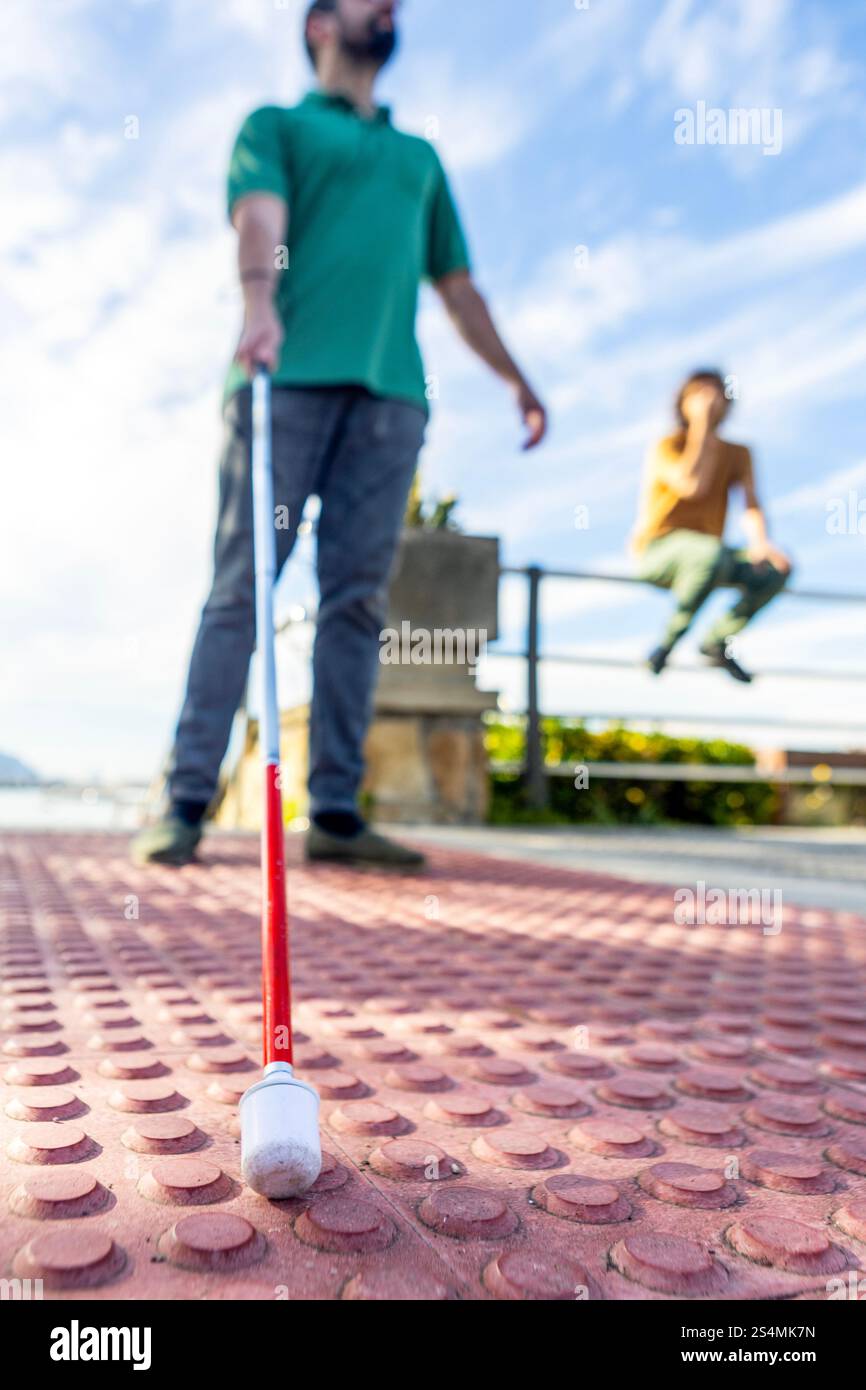A blind man uses a white cane to walk confidently on a tactile path ...