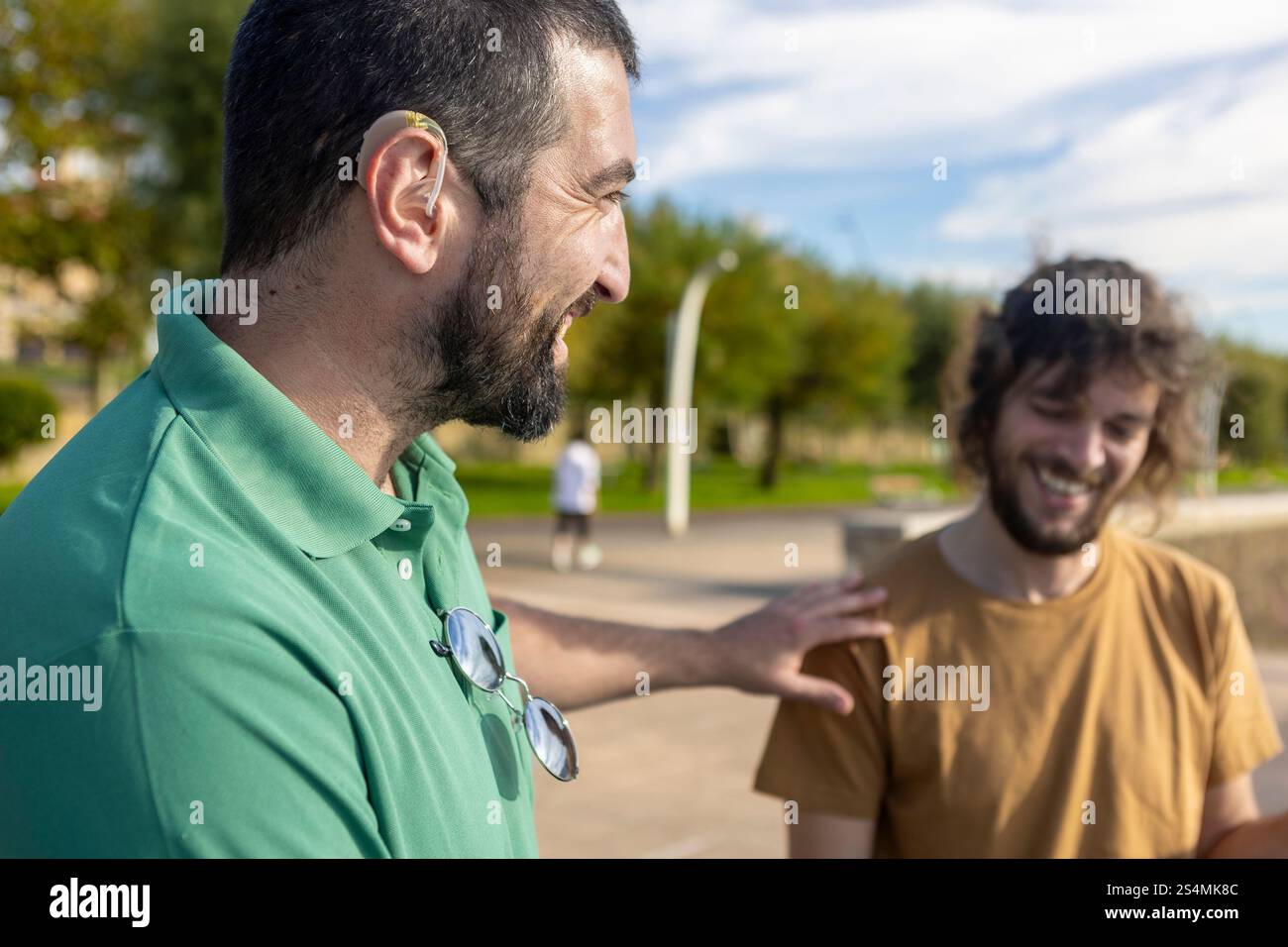 A blind man in a green shirt, wearing a hearing aid, shares a joyful ...