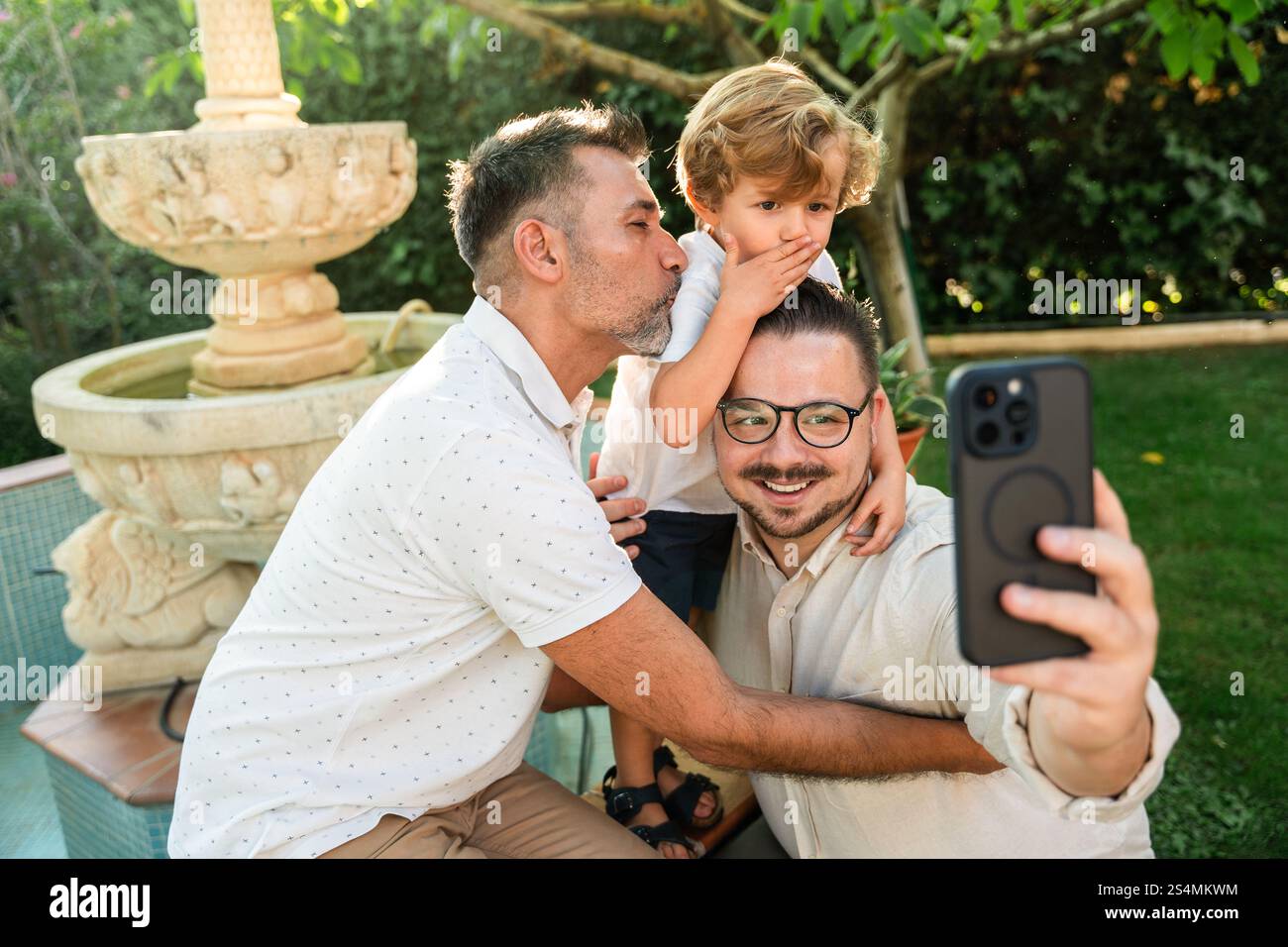 A joyful gay couple takes a selfie with their young son in a lush ...