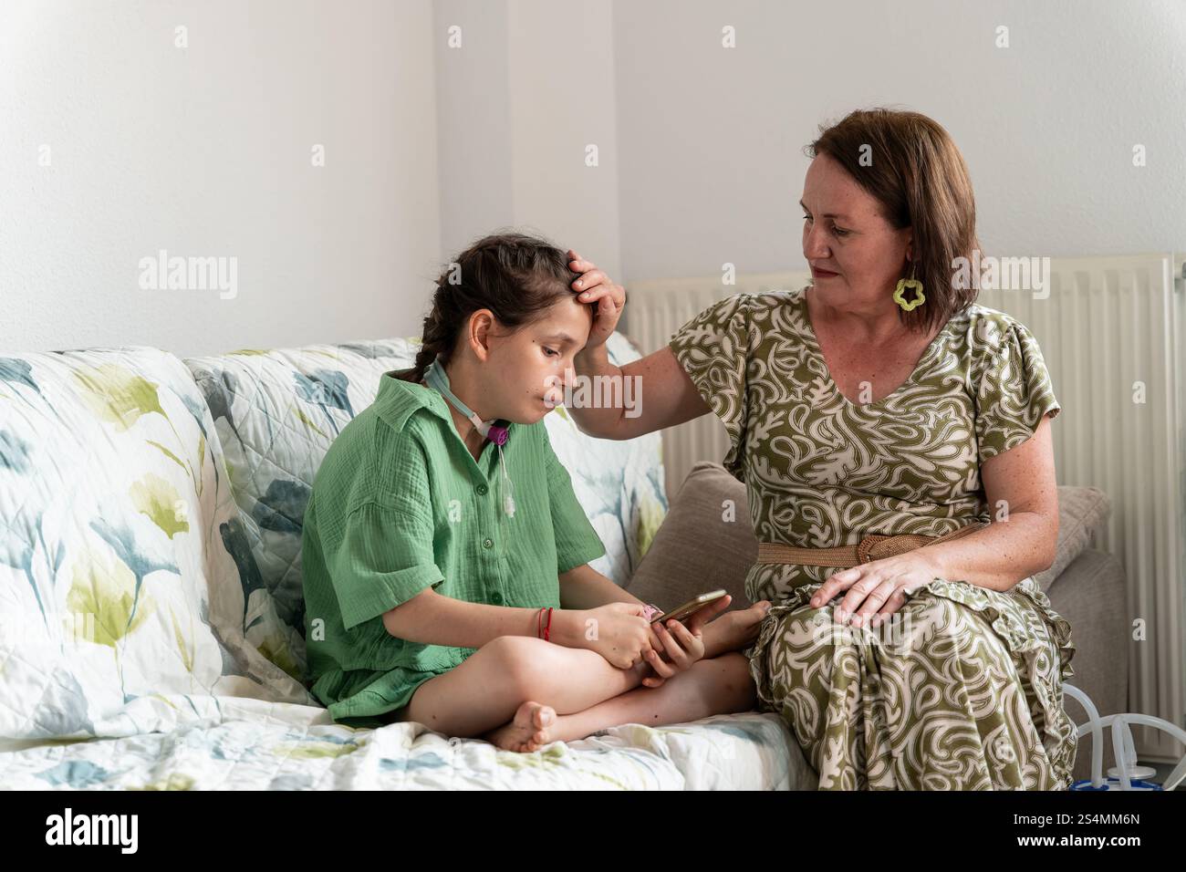 A caring family scene featuring a girl with a tracheostomy sitting beside a supportive mother ...