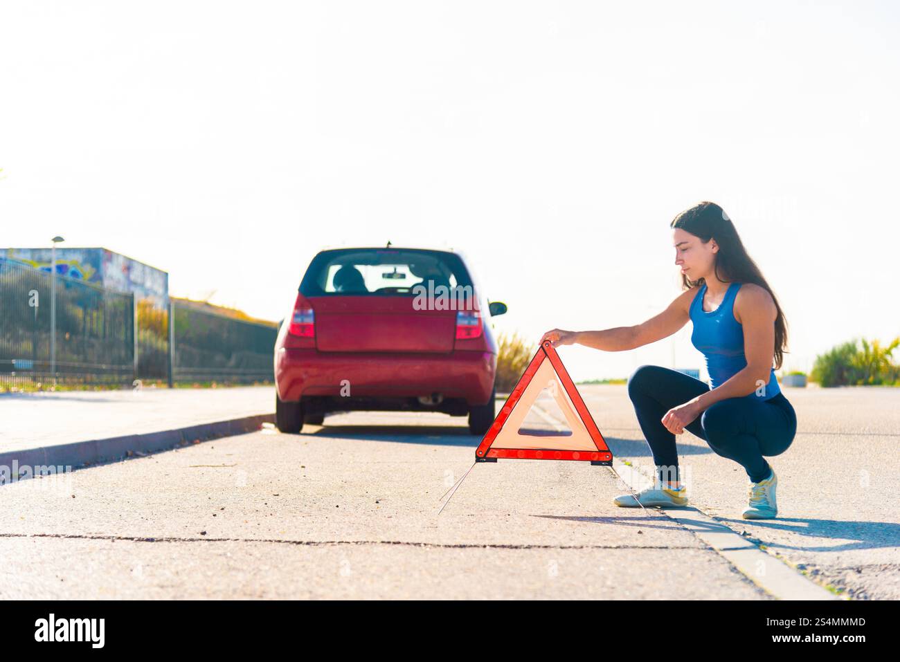 A young woman places a reflective warning triangle behind her car on a ...