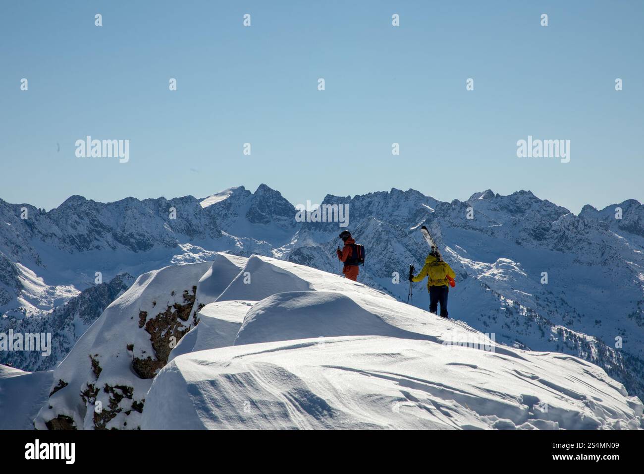 Two freeride skiers traverse a snowy ridge under a clear blue sky ...