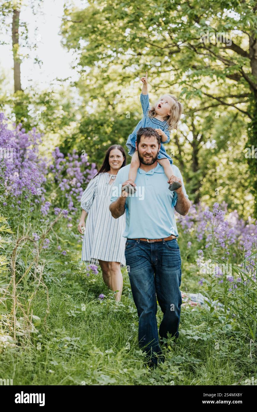 Child sits on dad's shoulders as family walks through park Stock Photo ...