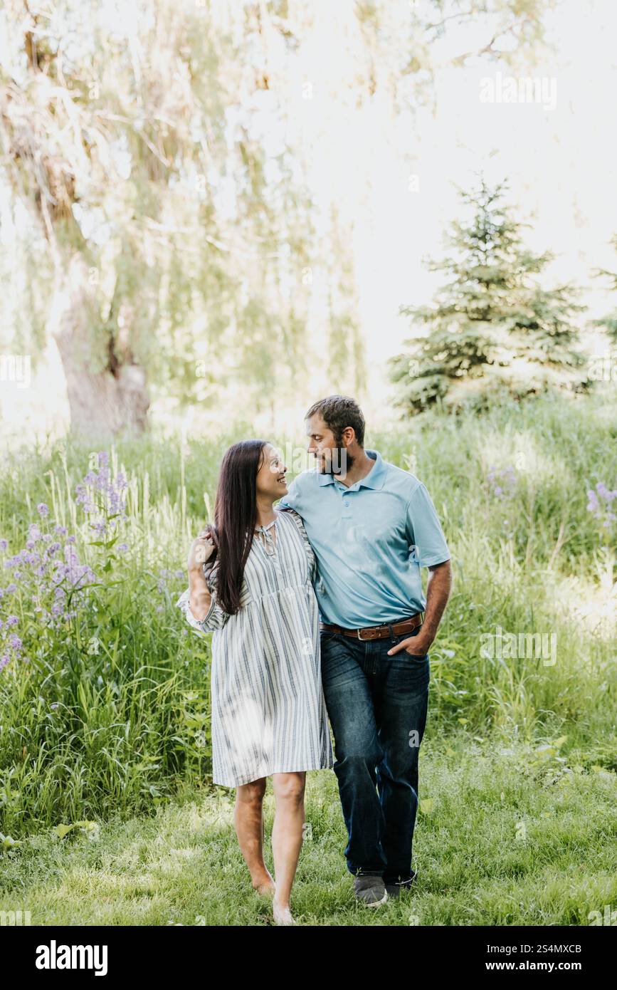 Man and wife walk with arms wrapped around each other through park ...