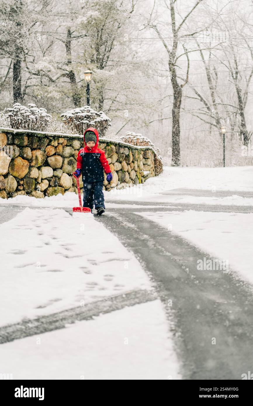 Child in red coat shoveling snow on driveway in a snowy landscape Stock ...