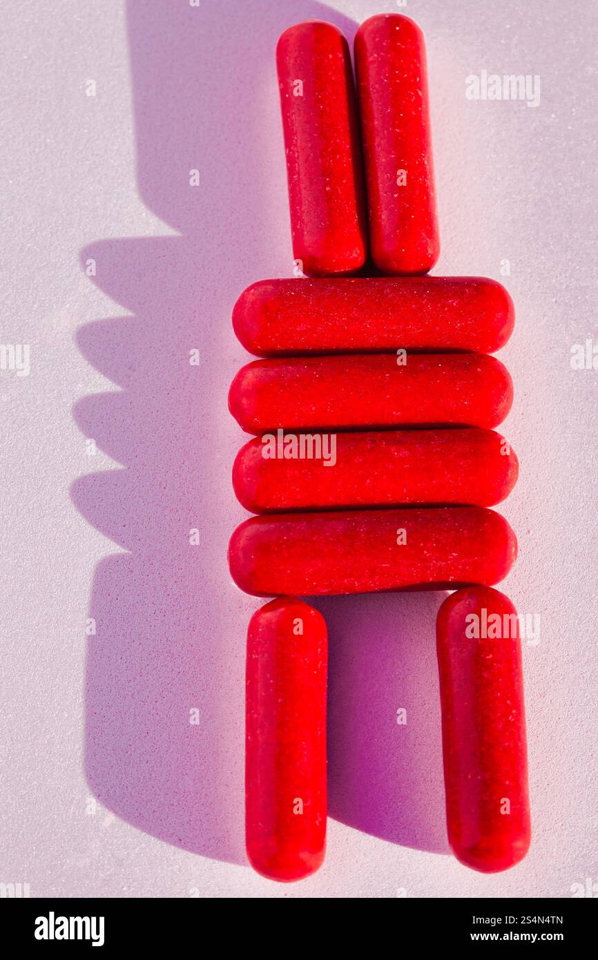 Red candies arranged in a stacked formation on a pastel pink surface ...