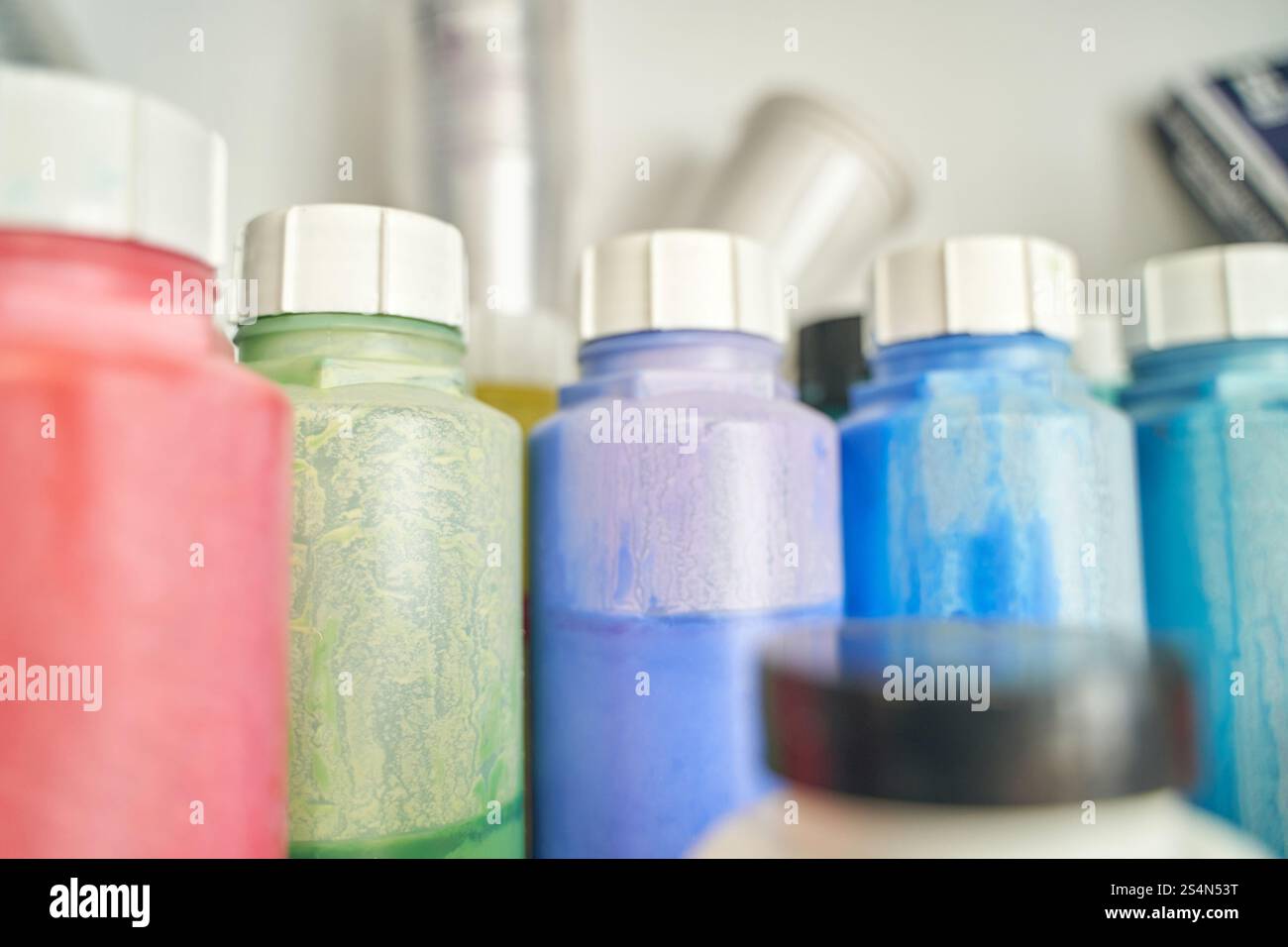 Colorful array of plastic paint bottles in a row on shelf closeup with ...